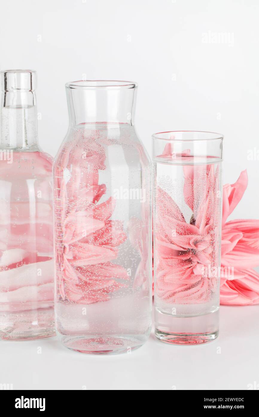 pink flowers distorted through water in glasses and bottle on white ...