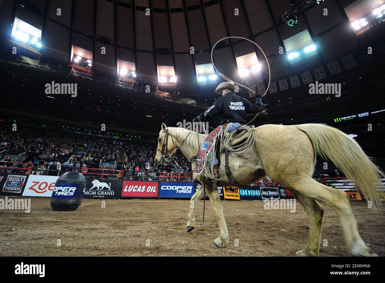 A rodeo horse walks across the stadium as his rider twirls his lasso ...