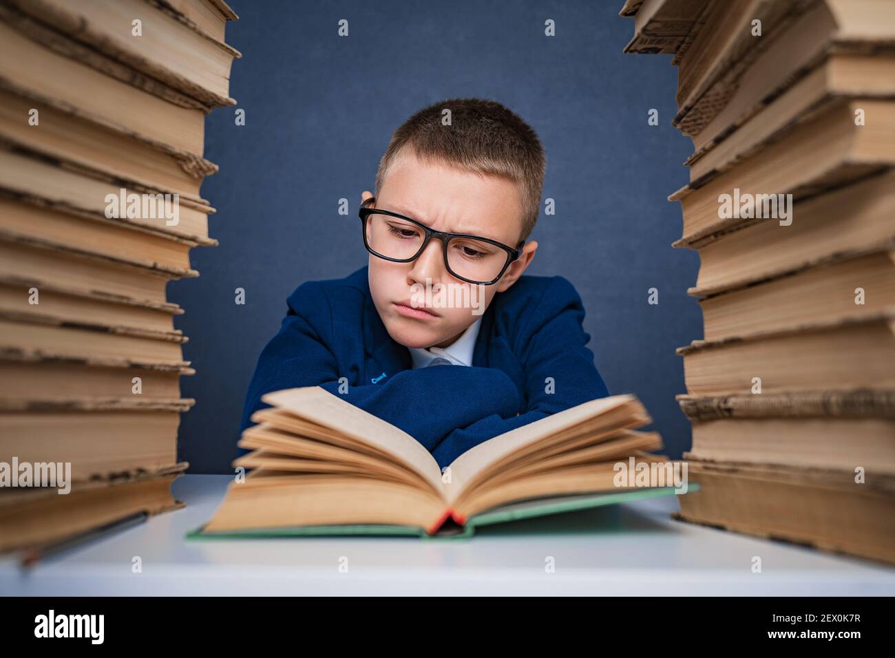 Smart boy in glasses sitting between two piles of books and read book ...