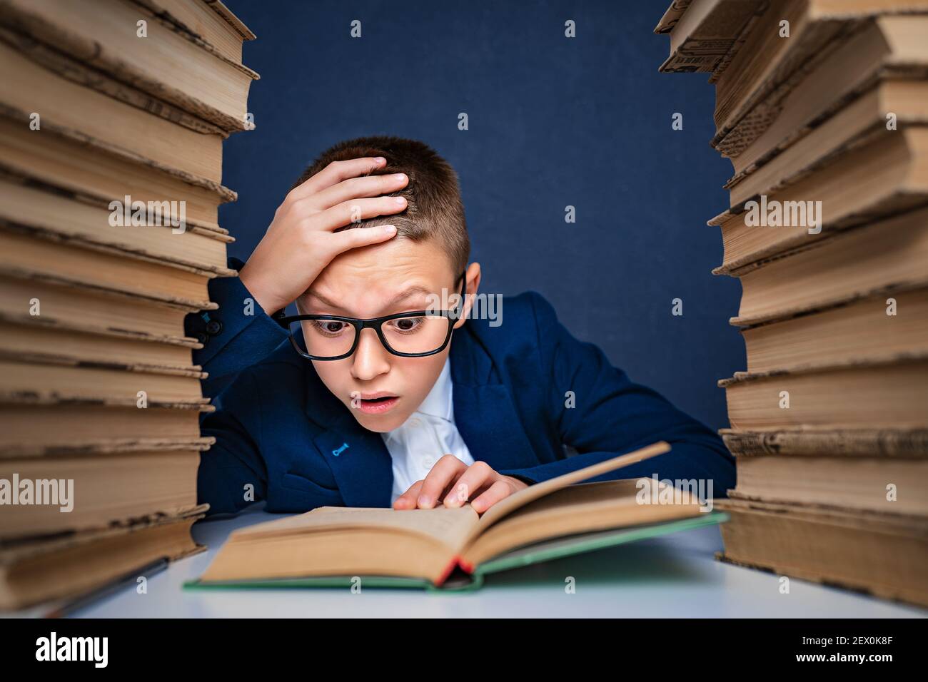 Smart boy in glasses sitting between two piles of books and read book ...