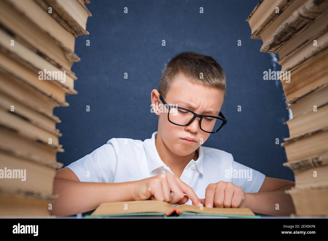 Smart boy in glasses sitting between two piles of books and read book ...