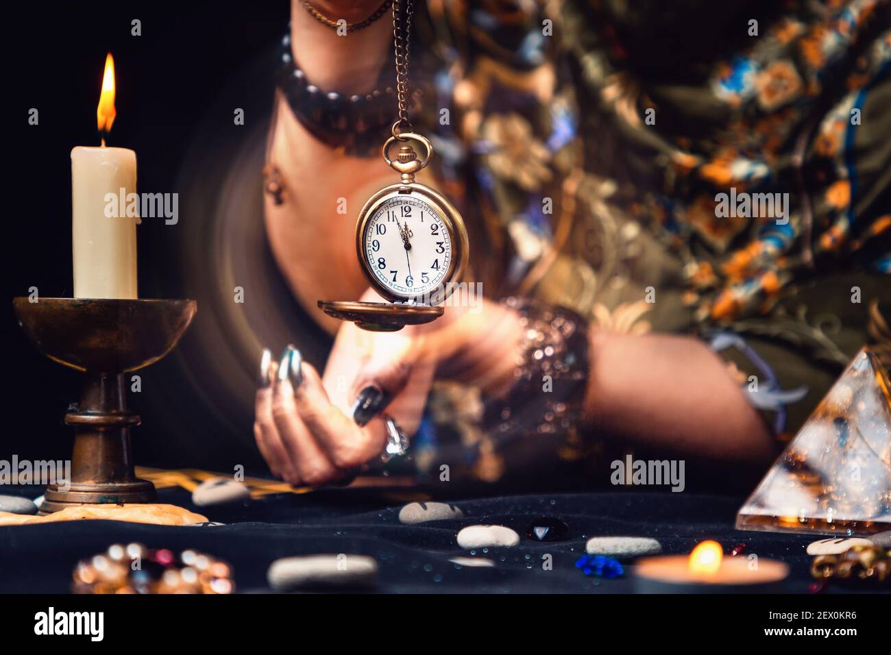 A fortune teller holds a watch on a chain in her hands, guessing for ...