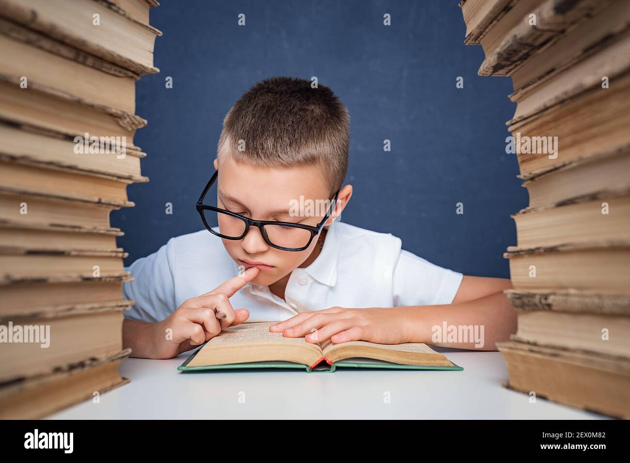 Smart boy in glasses sitting between two piles of books and read book ...