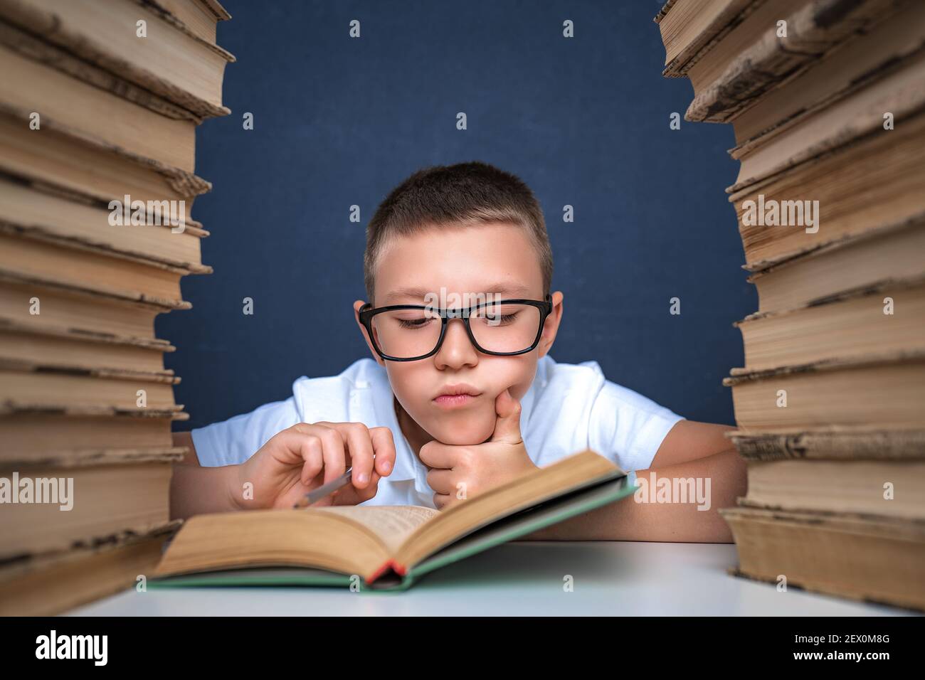 Smart boy in glasses sitting between two piles of books and read book ...
