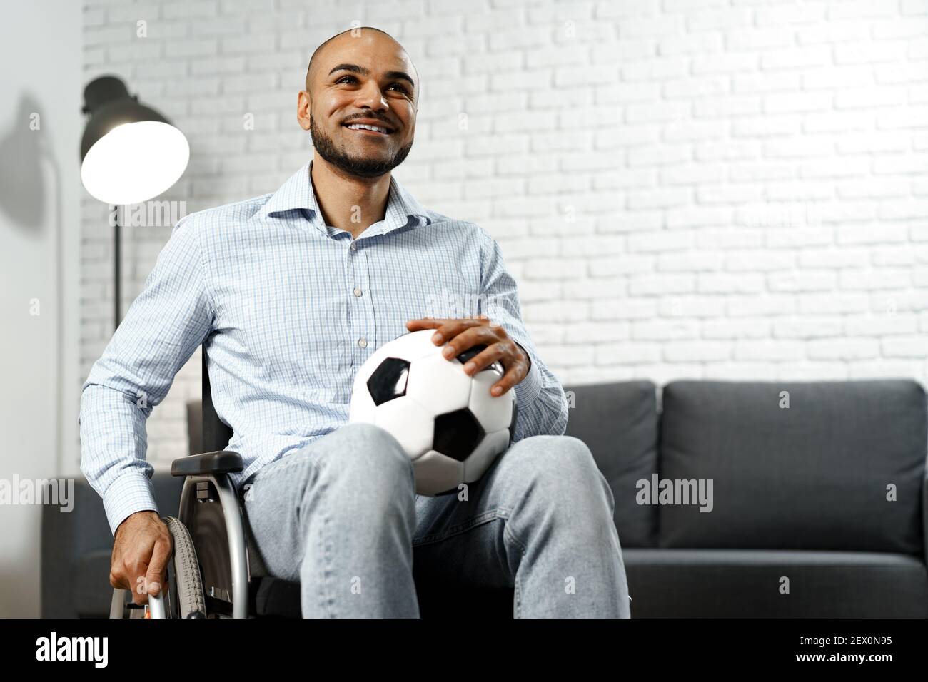 Happy young disabled man in wheelchair holding soccer ball and smiling ...