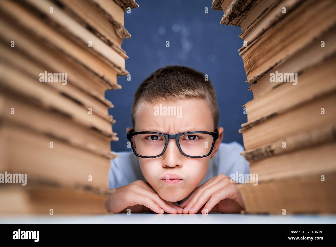 School boy in glasses sitting between two piles of books and look at ...