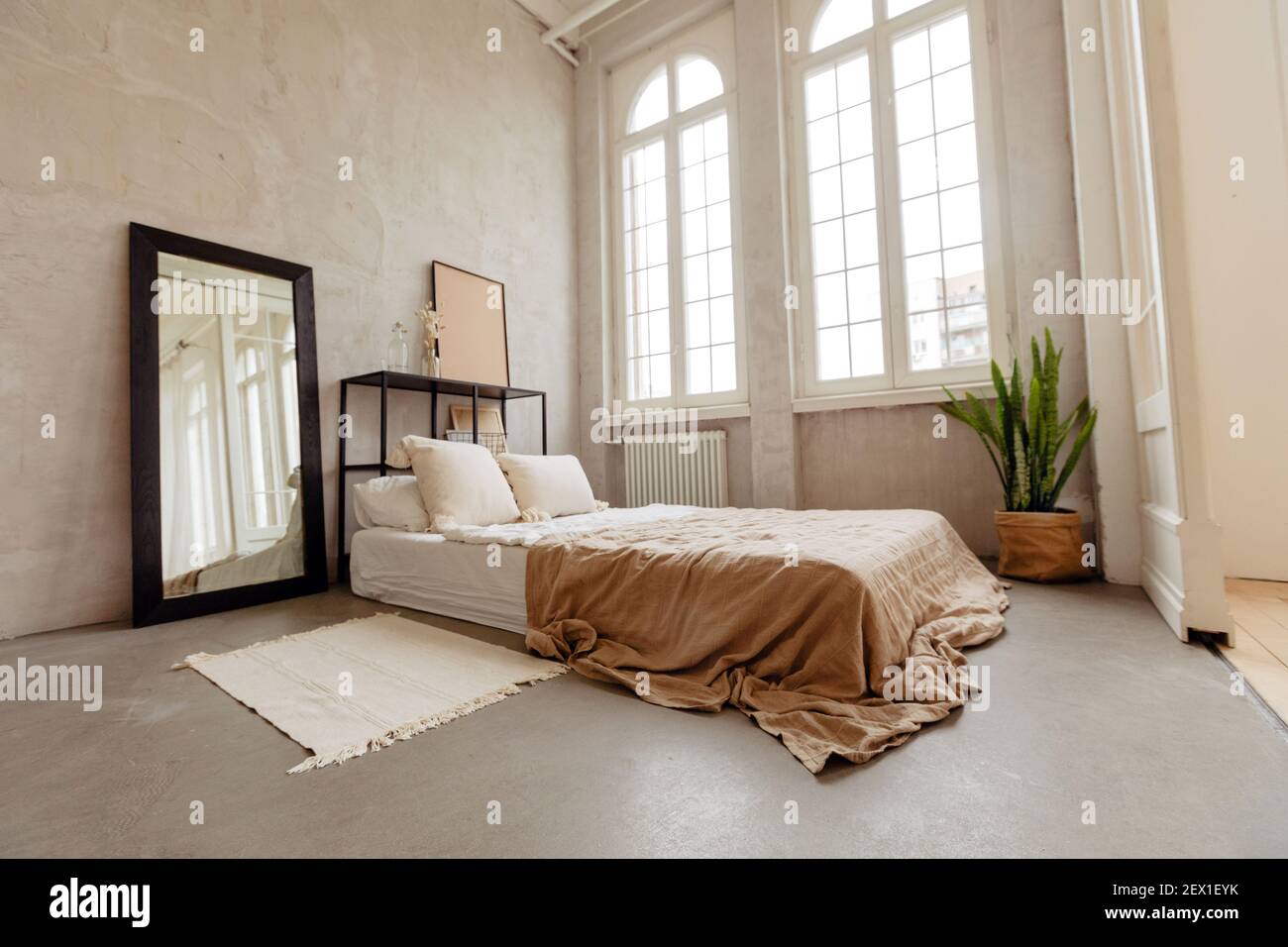 Empty wide bed with soft pillows and cute linens in big room with light ...