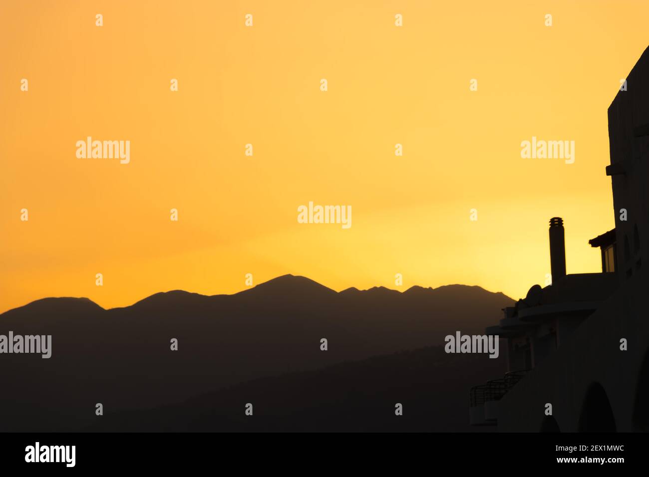 A scenic view of a wall of a house against a mountainous and golden sky ...