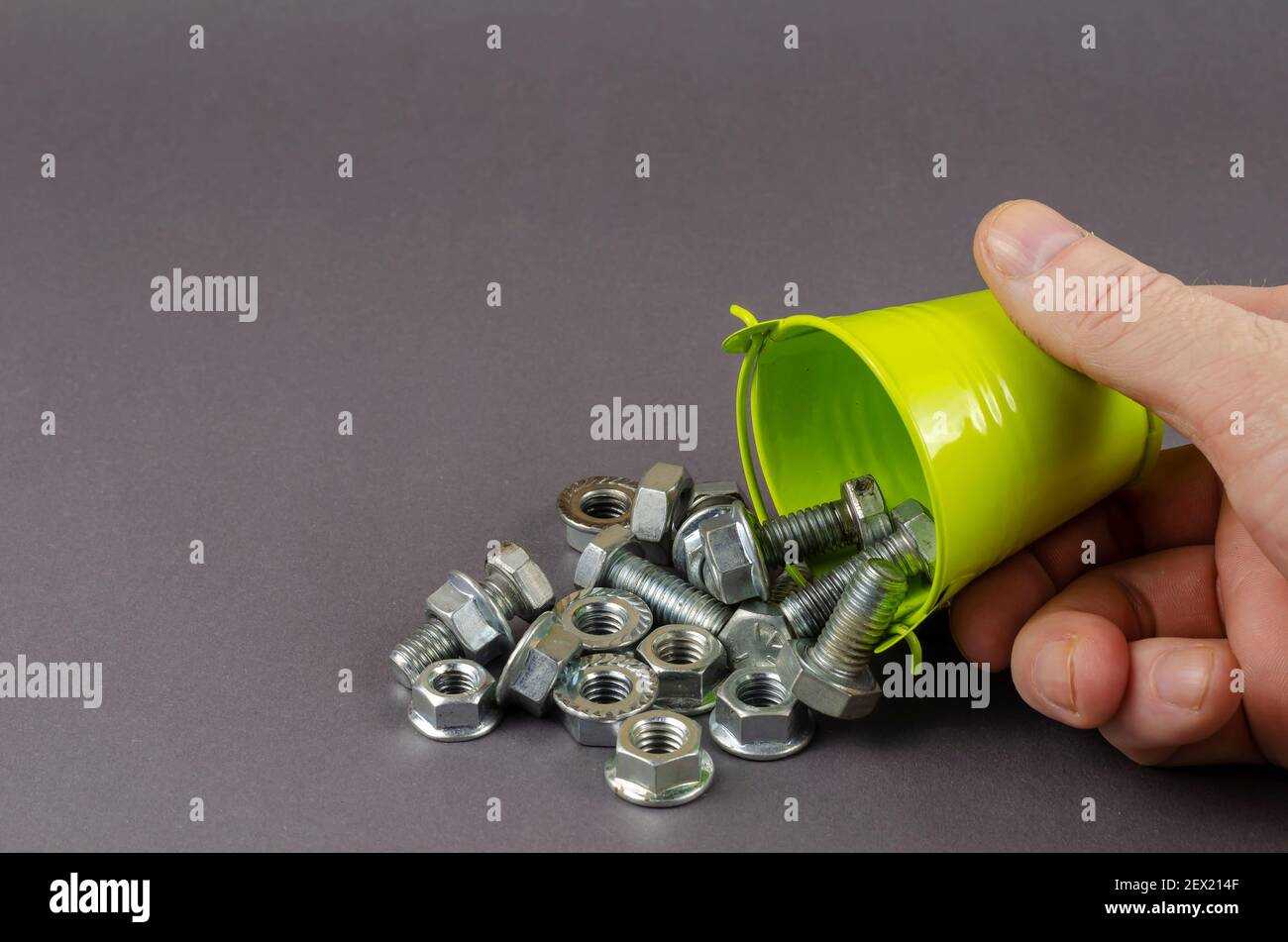 Bolts, nuts, hand and a small green bucket on a gray background. A man ...