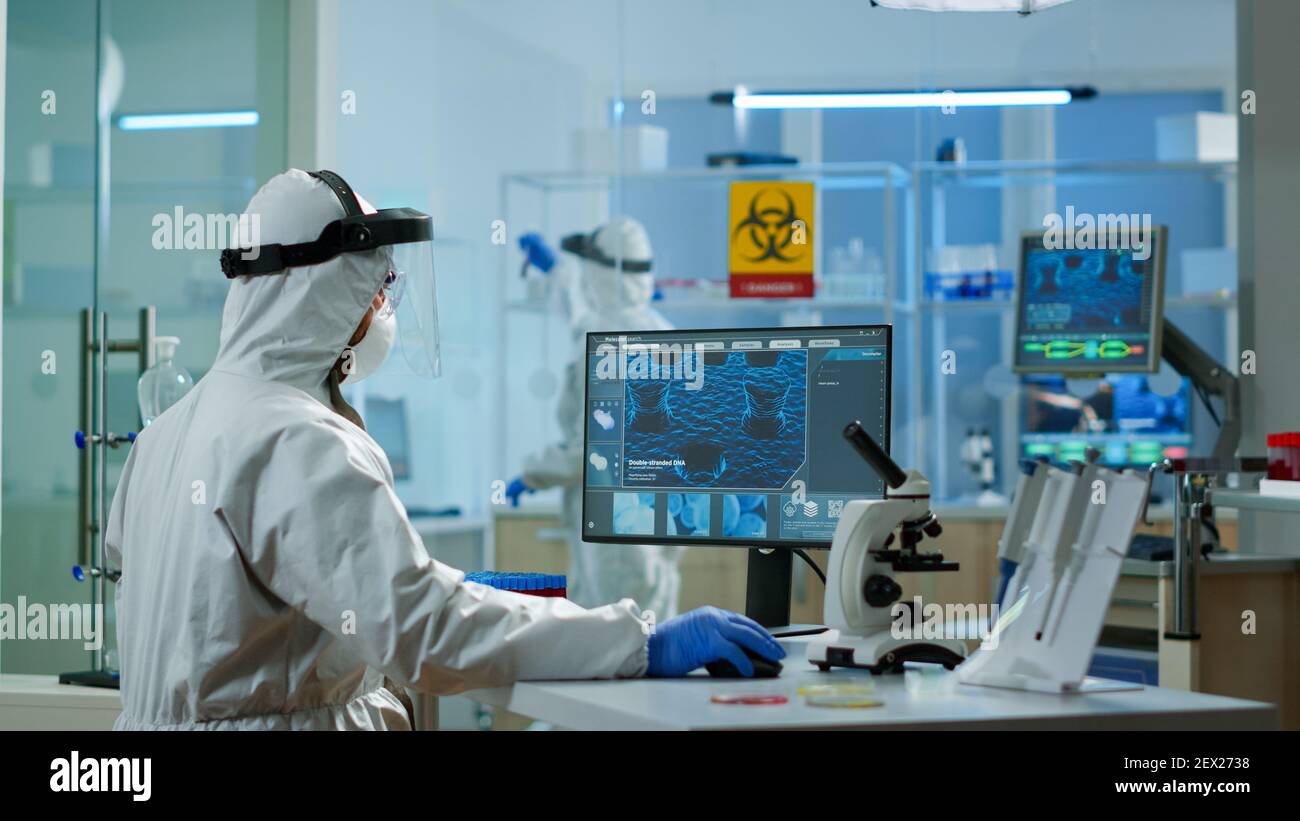 Medical scientist in ppe suit working with DNA scan image typing on pc ...