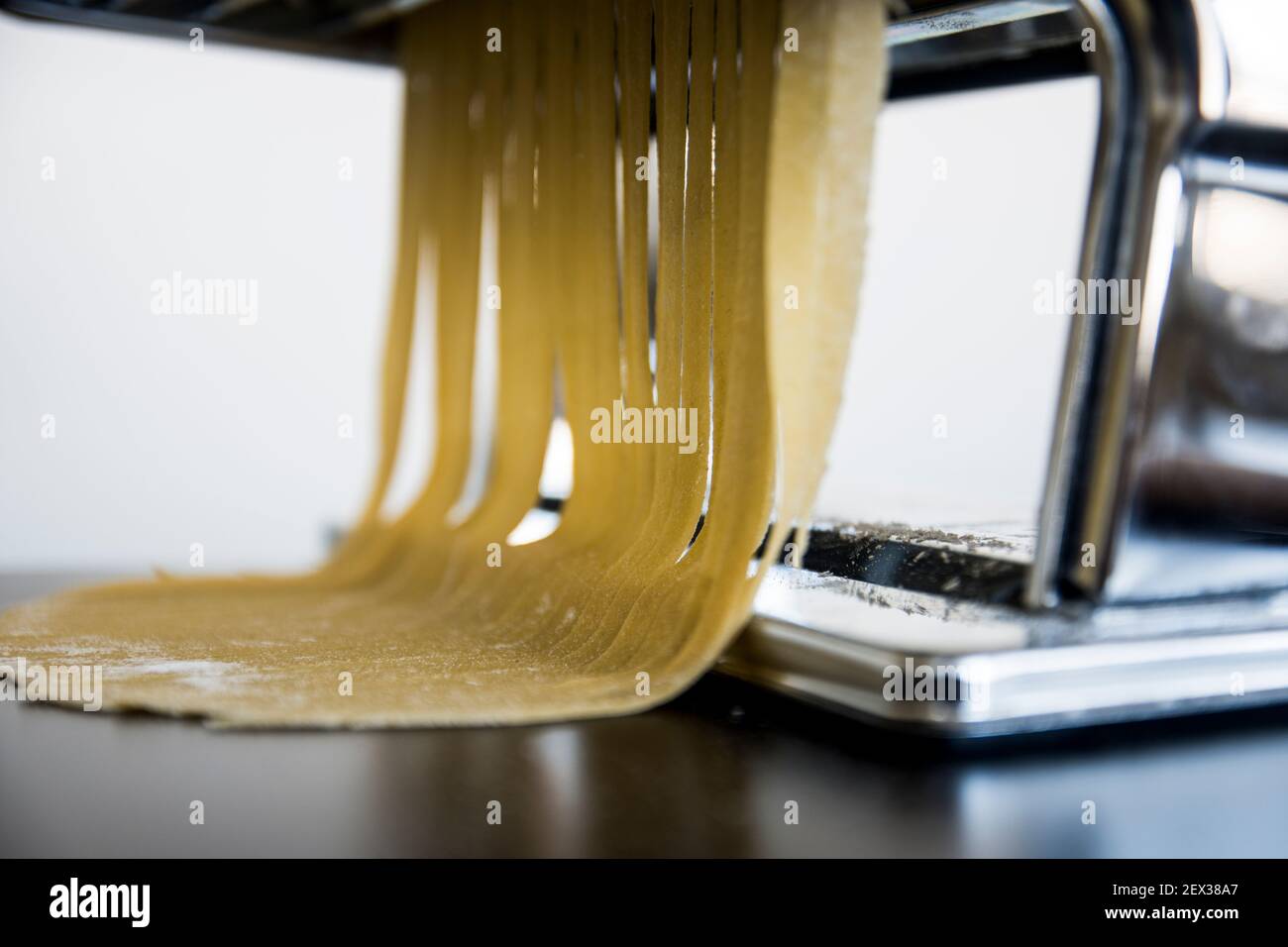Preparing homemade fettuccine on pasta machine. Cutting raw dough into ...
