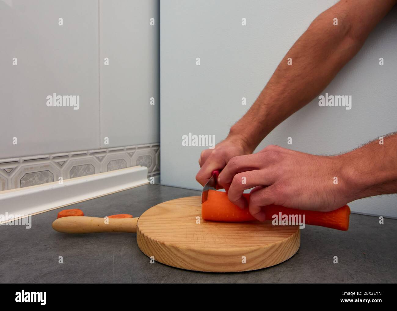 A wide-angle shot of a carrot being cut on a wooden cutting board in ...