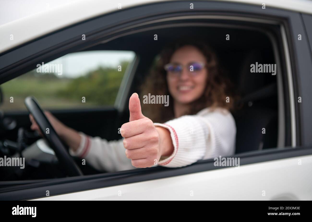Young woman driving making a thumbs up gesture with her hand. Concept ...