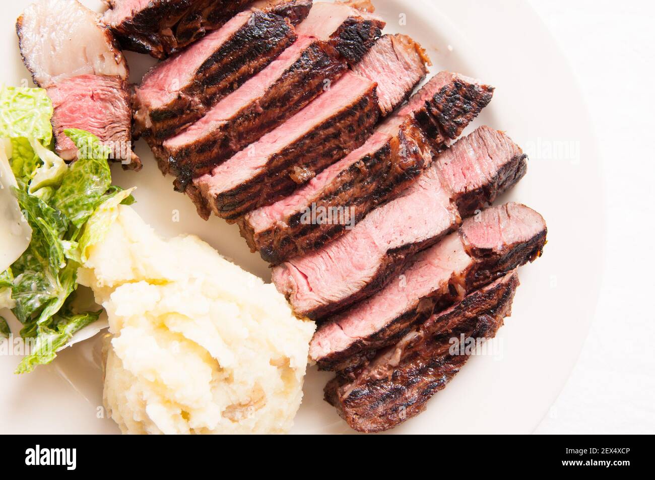 sliced rare beef rib eye steak with caesar salad and mashed potato ...