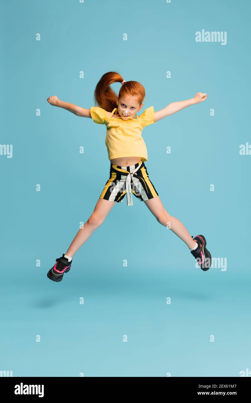 Jumping high. Happy, smiley little caucasian girl isolated on blue ...