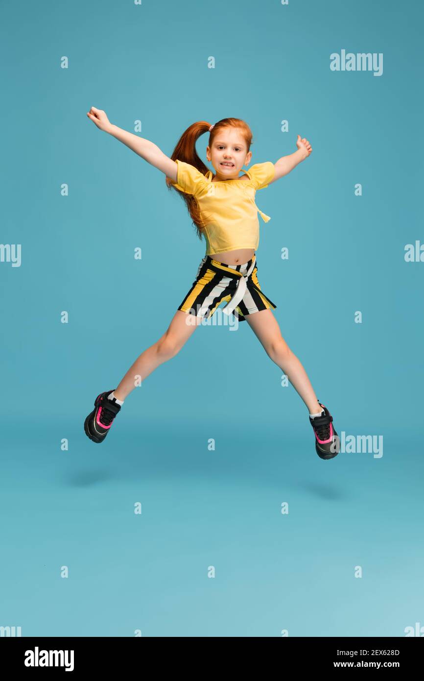 Jumping high. Happy, smiley little caucasian girl isolated on blue ...