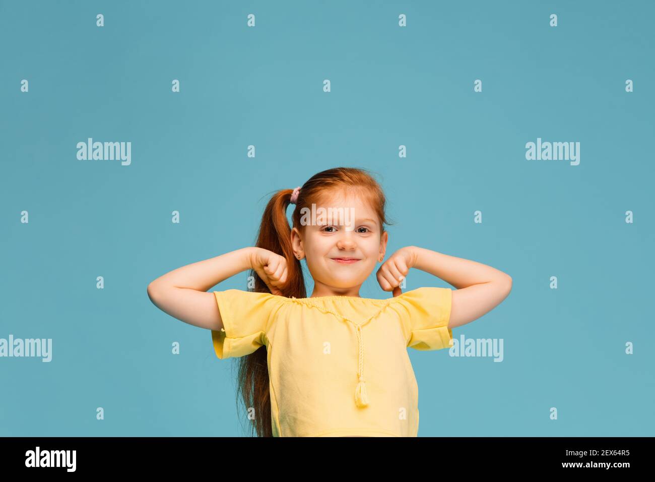 Strong, powerful. Happy, smiley little caucasian girl isolated on blue ...