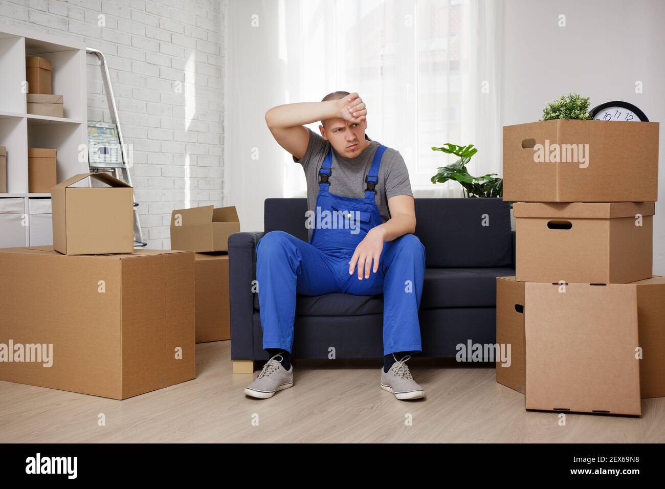 tired loader sitting on sofa in room after hard moving day Stock Photo ...
