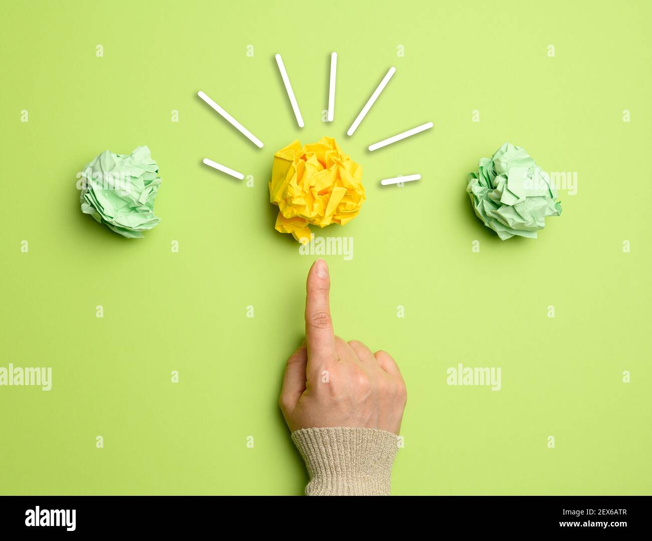 female hand points finger at yellow crumpled sheet of paper on green ...