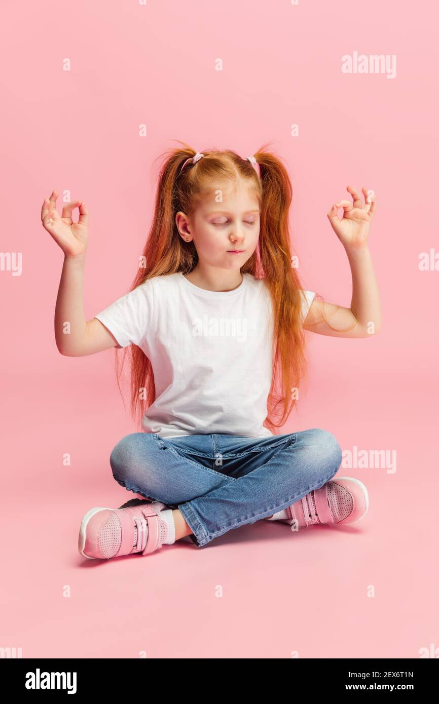 Meditation. Happy, smiley little caucasian girl isolated on pink studio ...