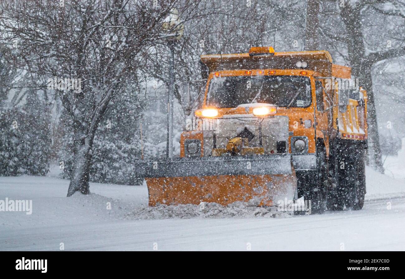 A yellow municipal snow plow is clearing a road while the snow is ...