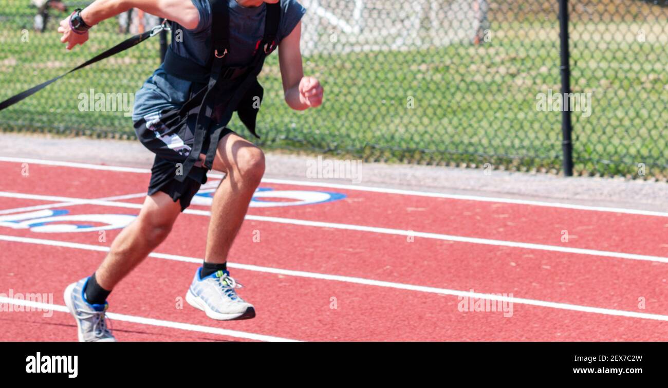 A high school track runner is pulling a wighted sled for resistance ...