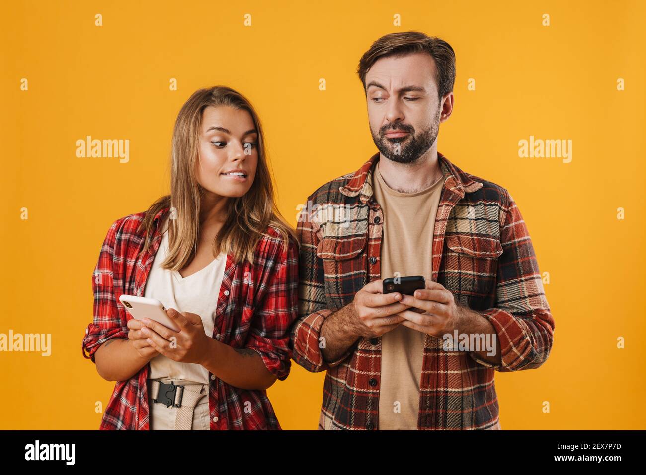 Focused charming couple posing with mobile phones and overlooking ...