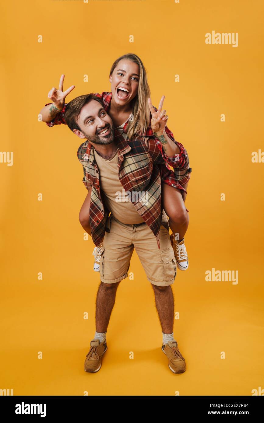 Young happy couple playing together piggyback isolated on yellow ...