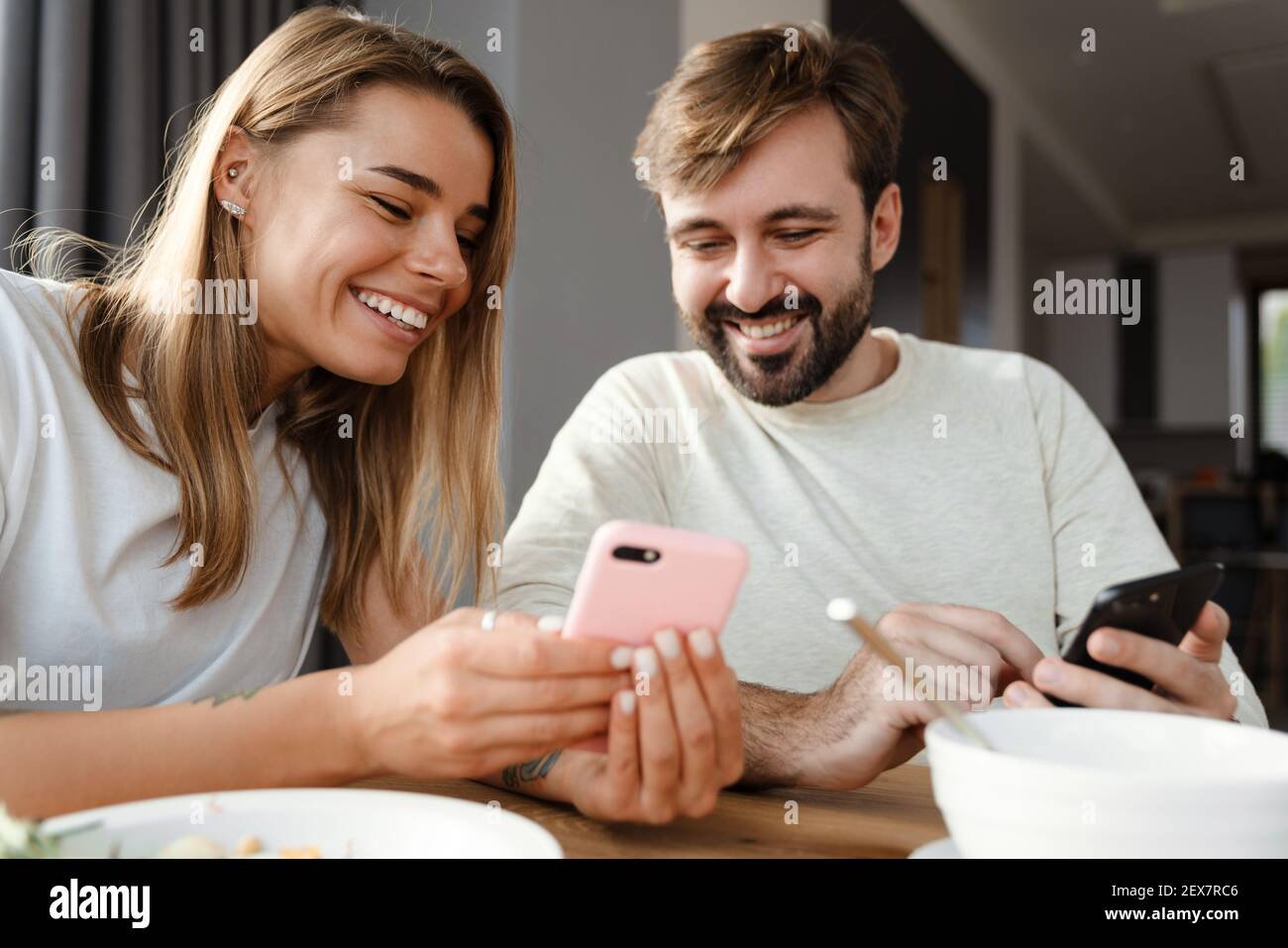 Happy young couple use mobile phone while having breakfast at home ...