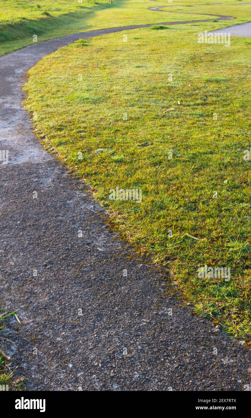Winding grey gravel footpath through green grass in a park on a sunny ...