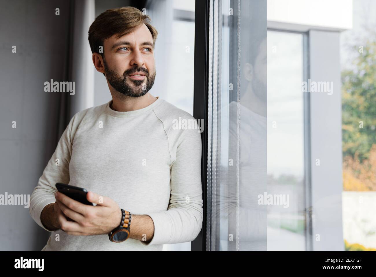 Handsome focused man using mobile phone while looking out window ...