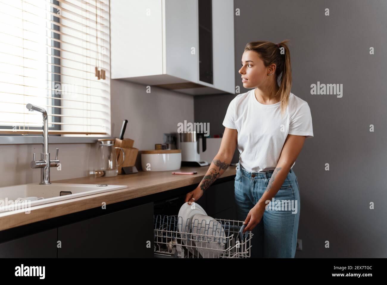Beautiful thinking girl looking out window while using dishwasher at ...