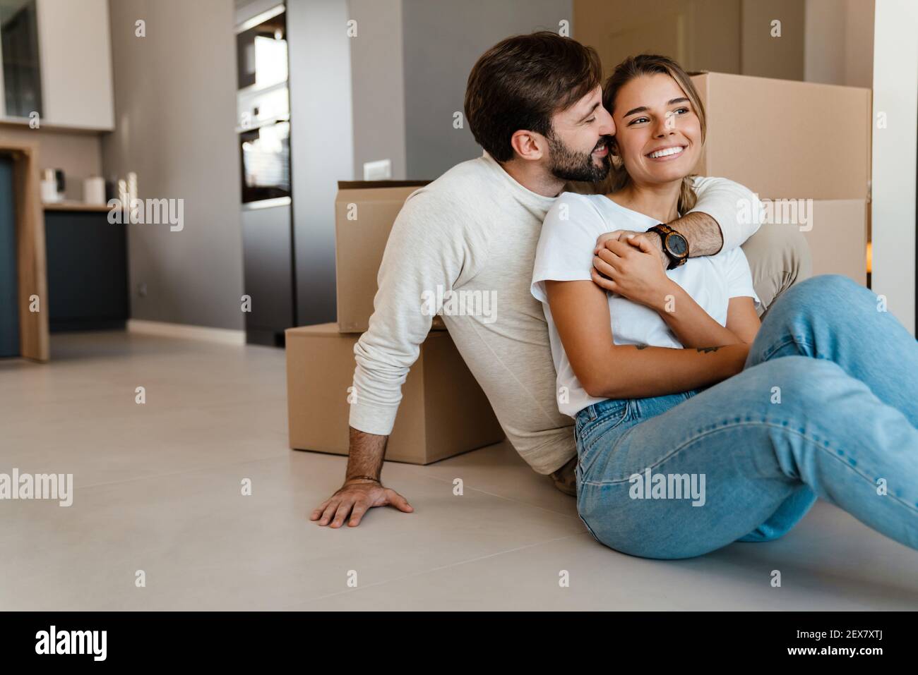 Beautiful couple smiling and hugging while sitting on floor with ...