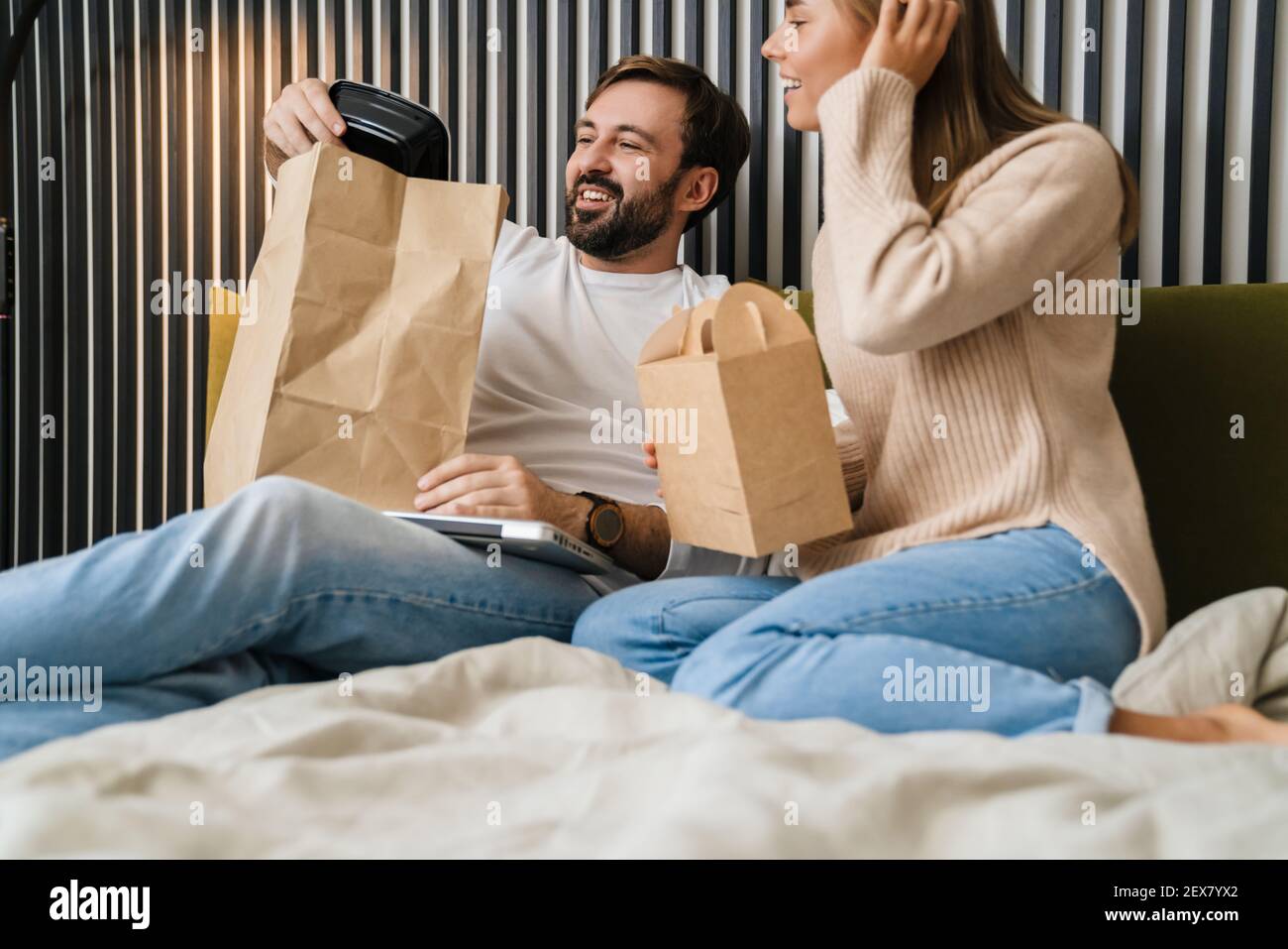 Couple eating take-away food in bedroom, sitting on bed Stock Photo - Alamy