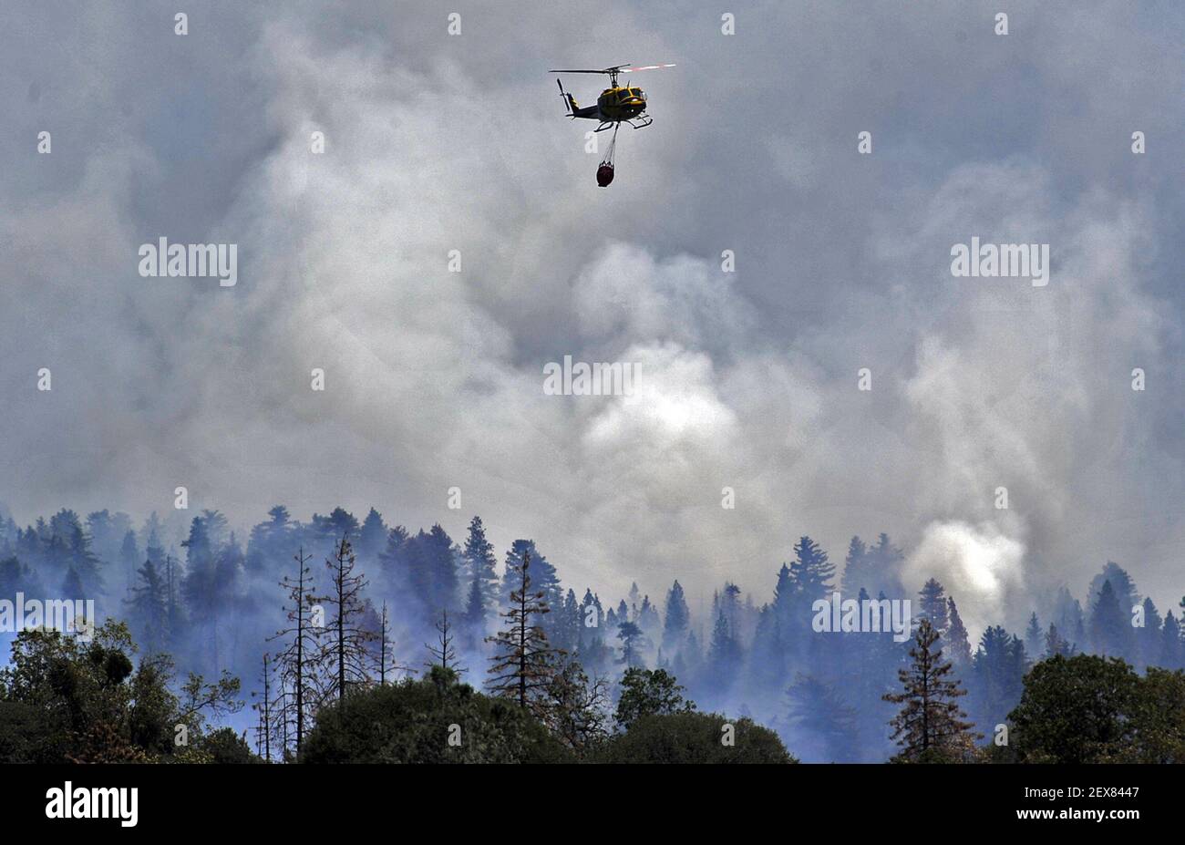 A helicopter flies away from a burning ridge after dropping water on ...