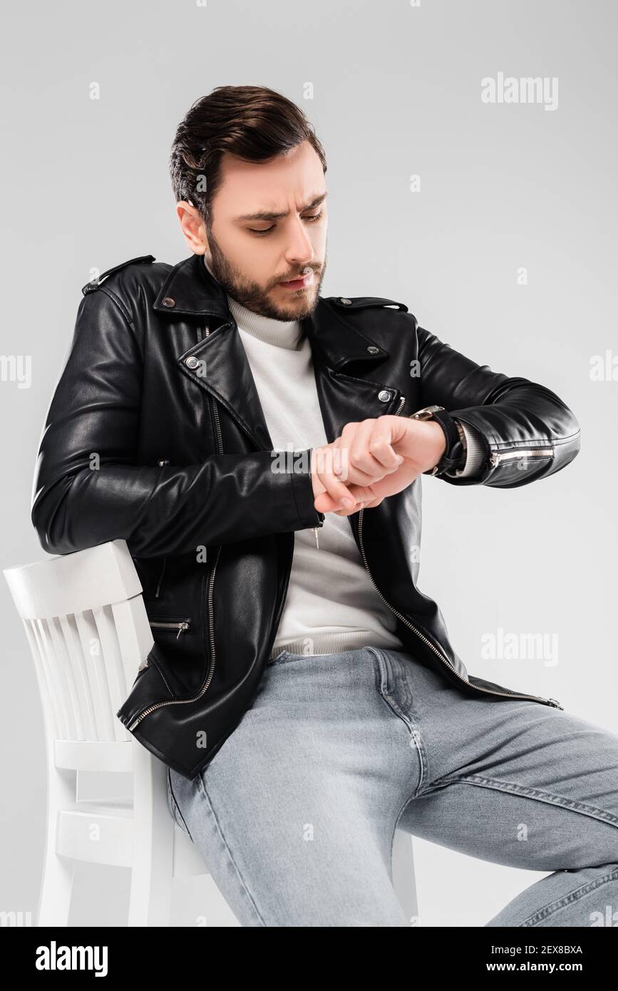 Man in leather jacket looking at wristwatch isolated on grey Stock ...