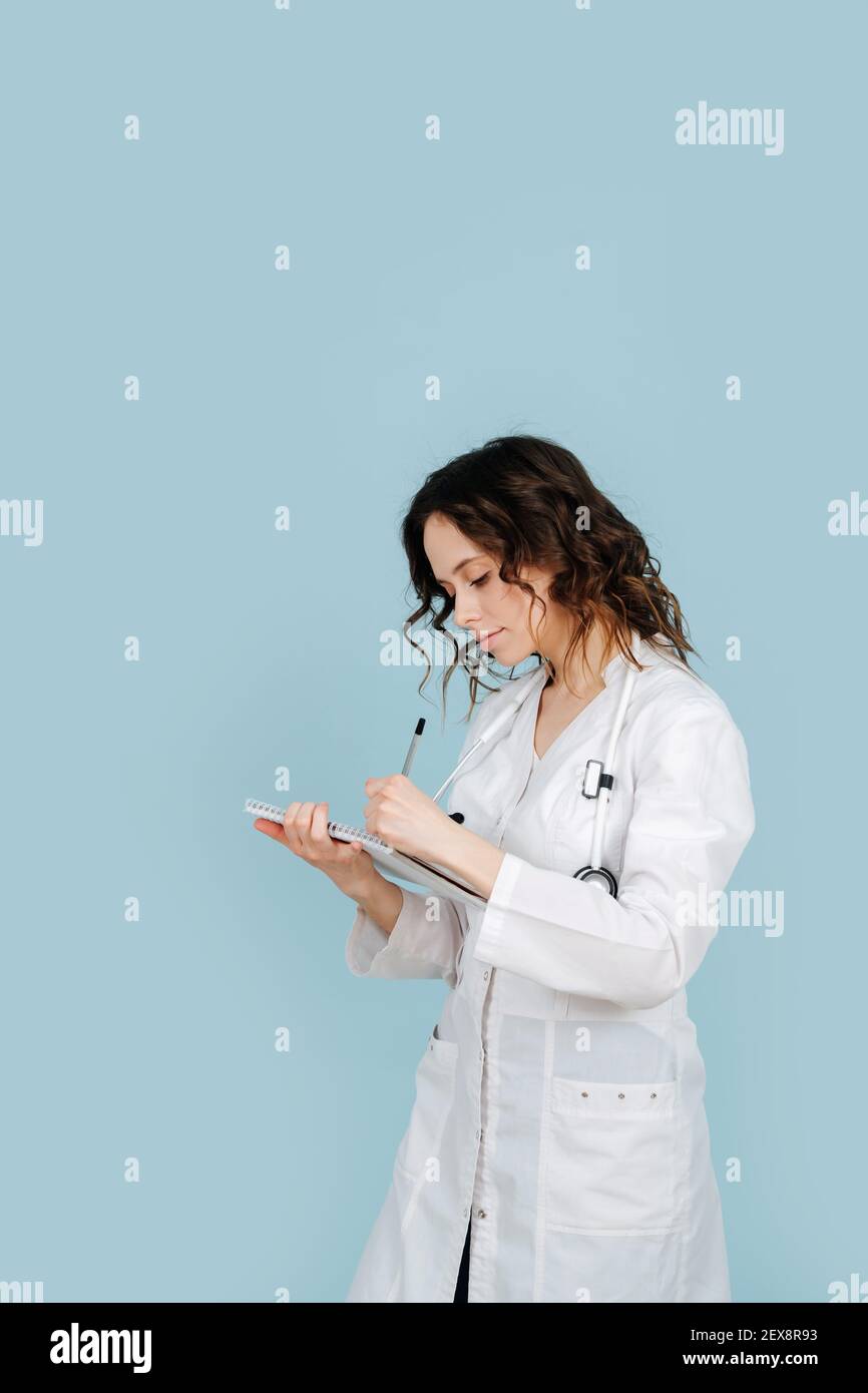 Young female nurse patiently writing in a notebook. Over blue ...