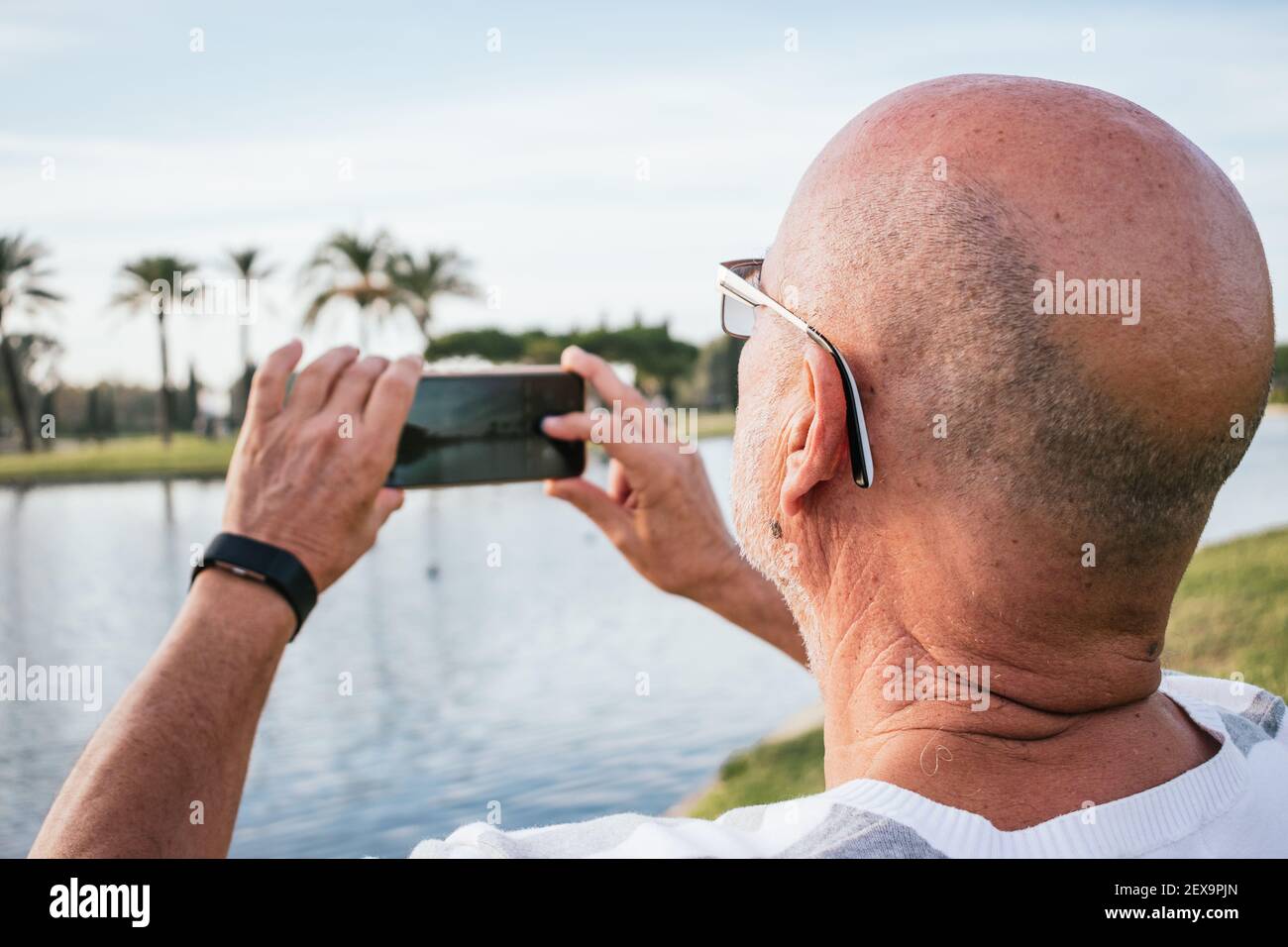 65-year-old man taking a photo with a smartphone in a park Stock Photo ...