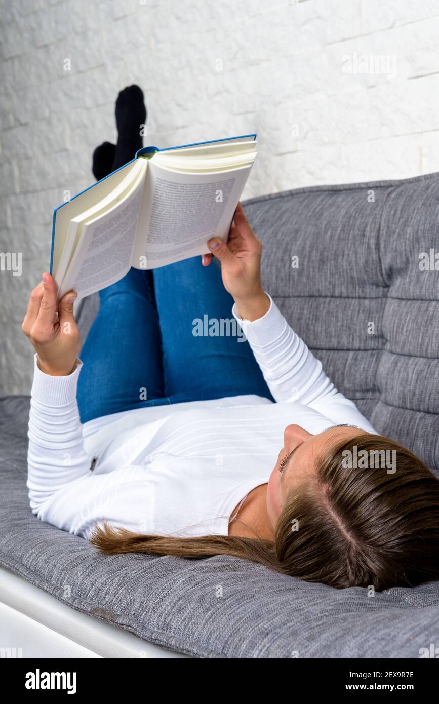 Student reading a book relaxed with legs up on the sofa in front of a ...