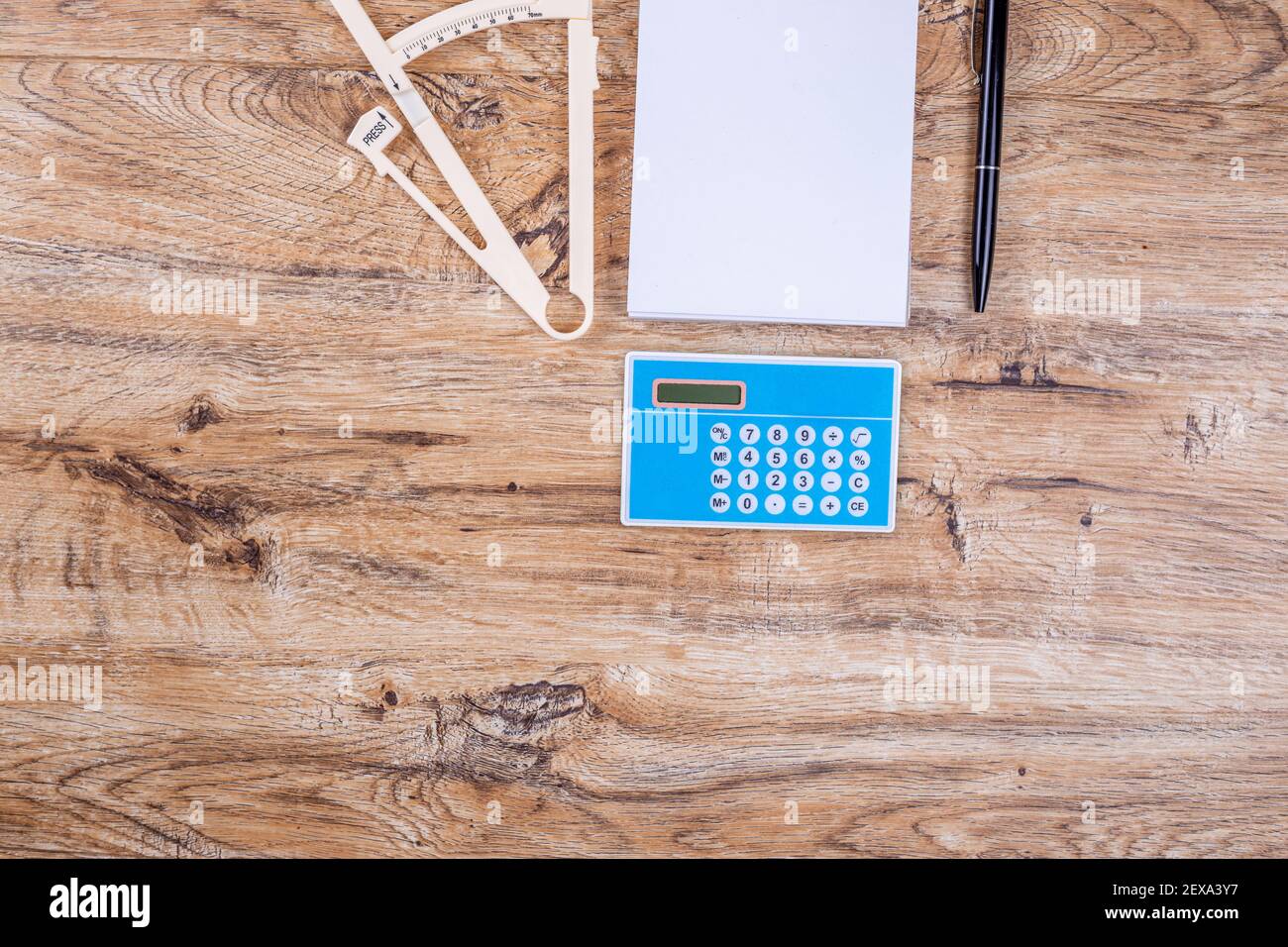 Blank sheet of notepad pen calculator and caliper on wooden table top ...
