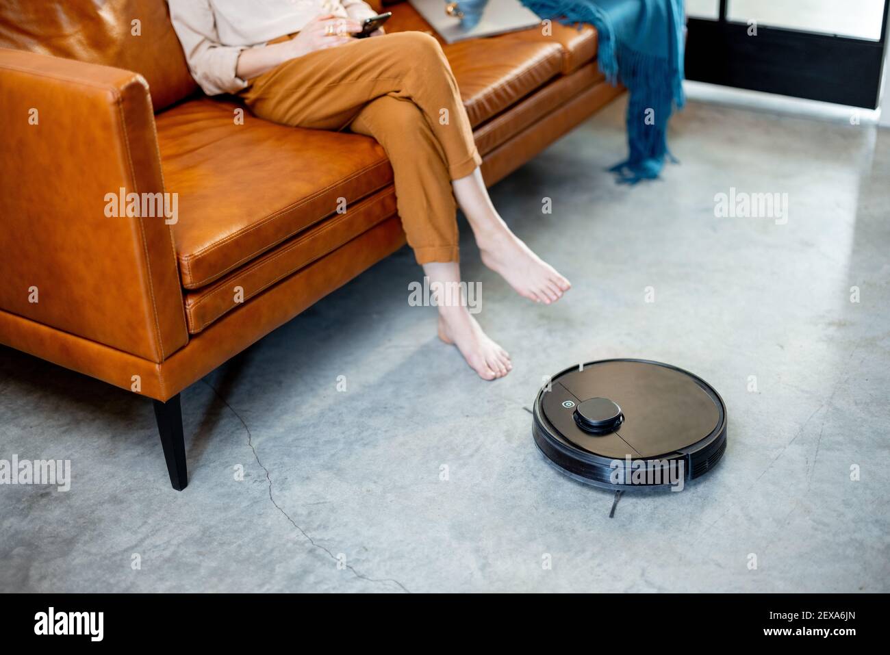 Black robotic vacuumer is cleaning the floor while pretty woman sitting ...
