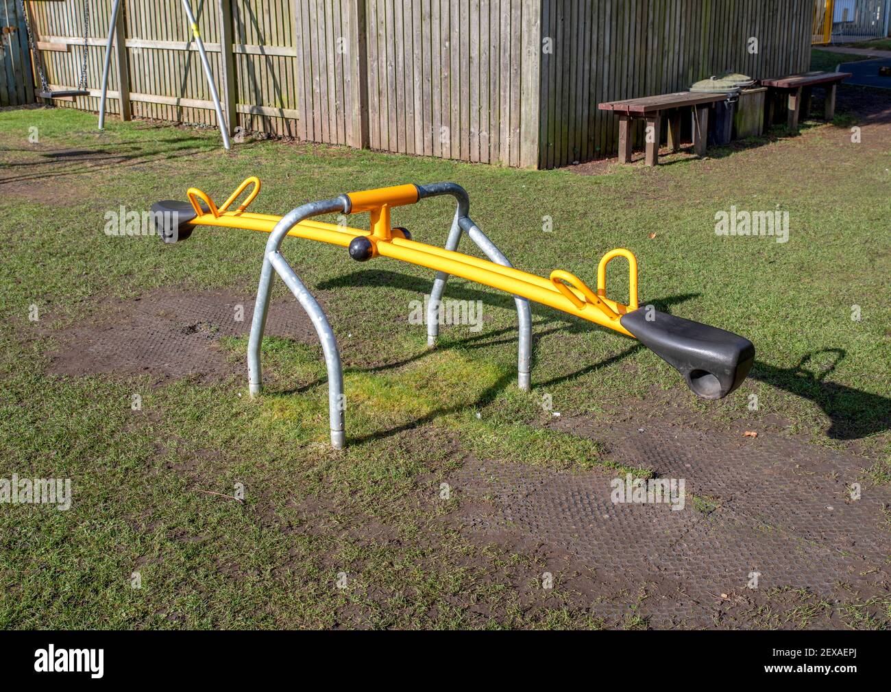 A yellow seesaw in a playground with grass and no people Stock Photo ...