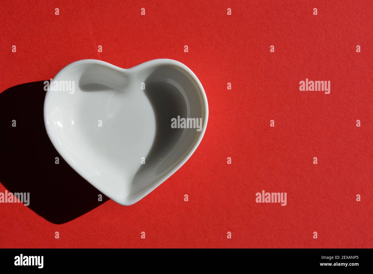 White ceramic heart shaped dish isolated on bright red background with ...