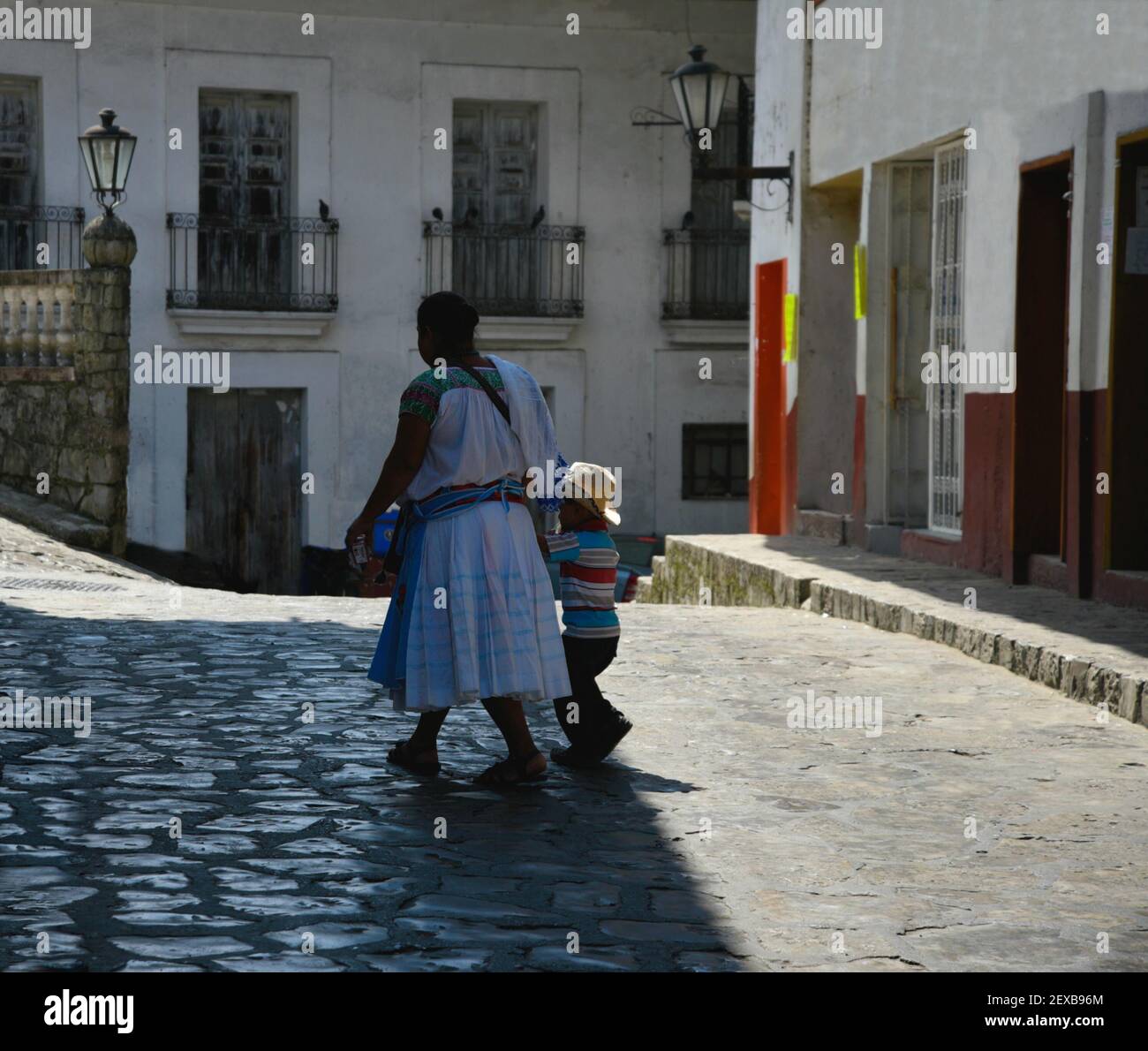 Indigenous Nahua woman with her child walking on the narrow cobblestone ...