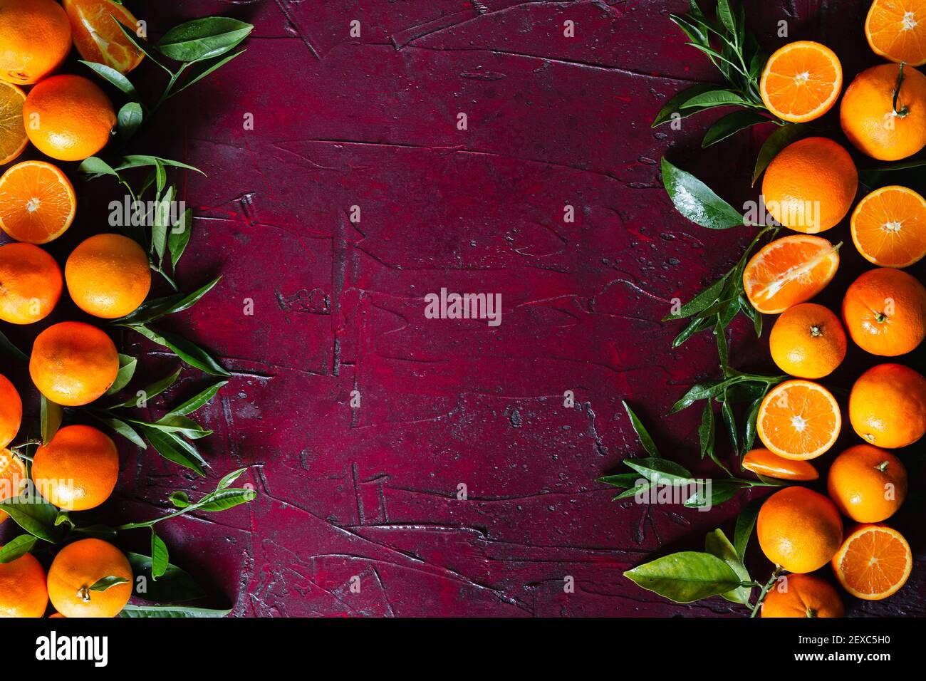 Orange tree leaves and fresh whole, halved, and quartered oranges are ...