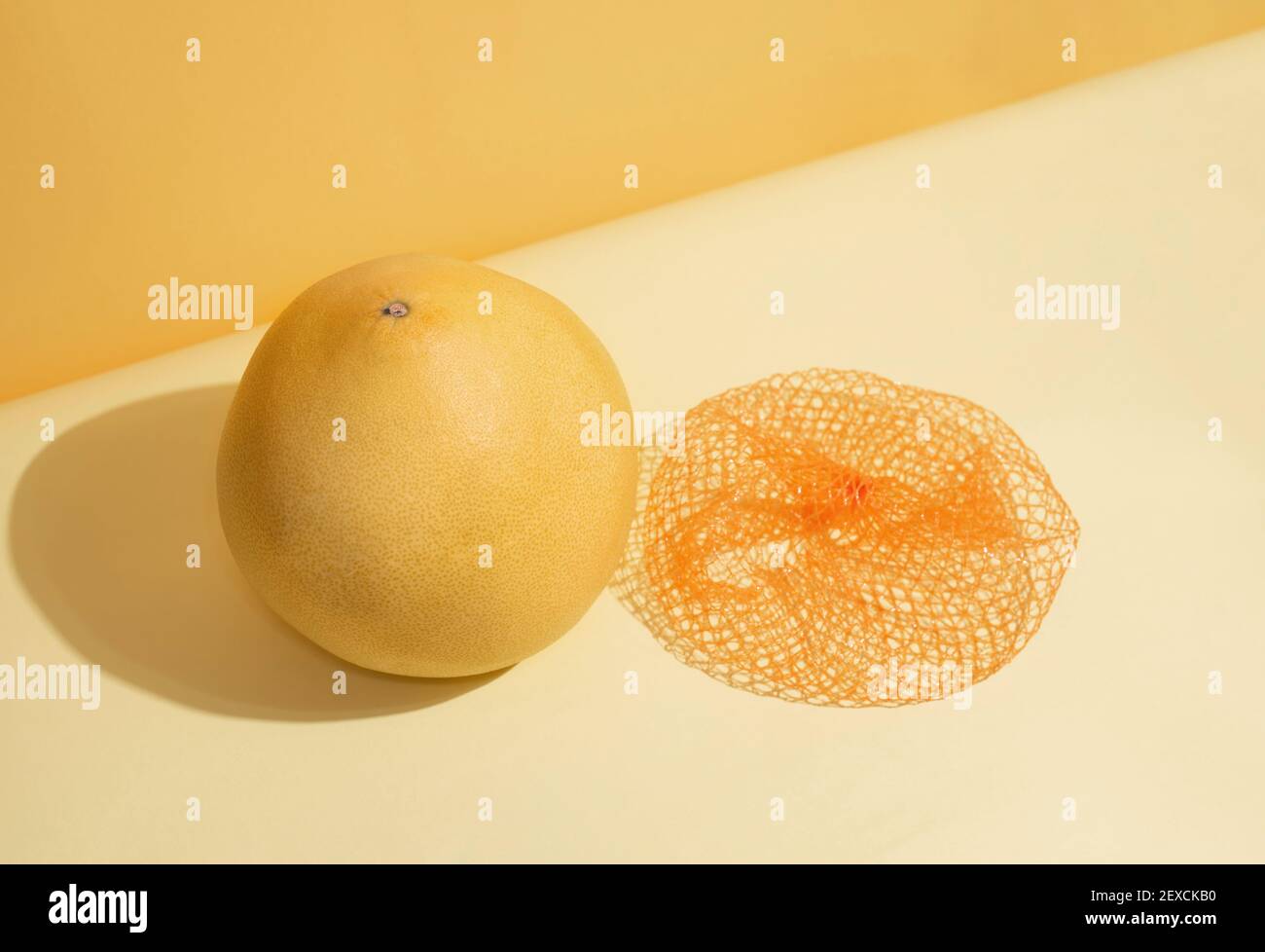 Yellow fresh pomelo and mesh packaging on a yellow and orange ...
