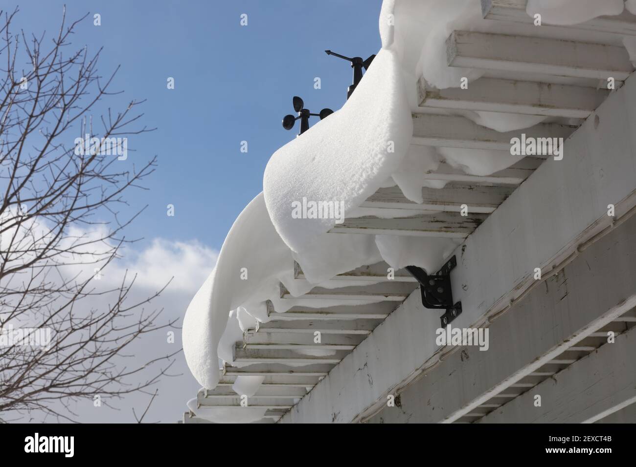 Waves of snow overhanging a pergola with a weather station on it after ...