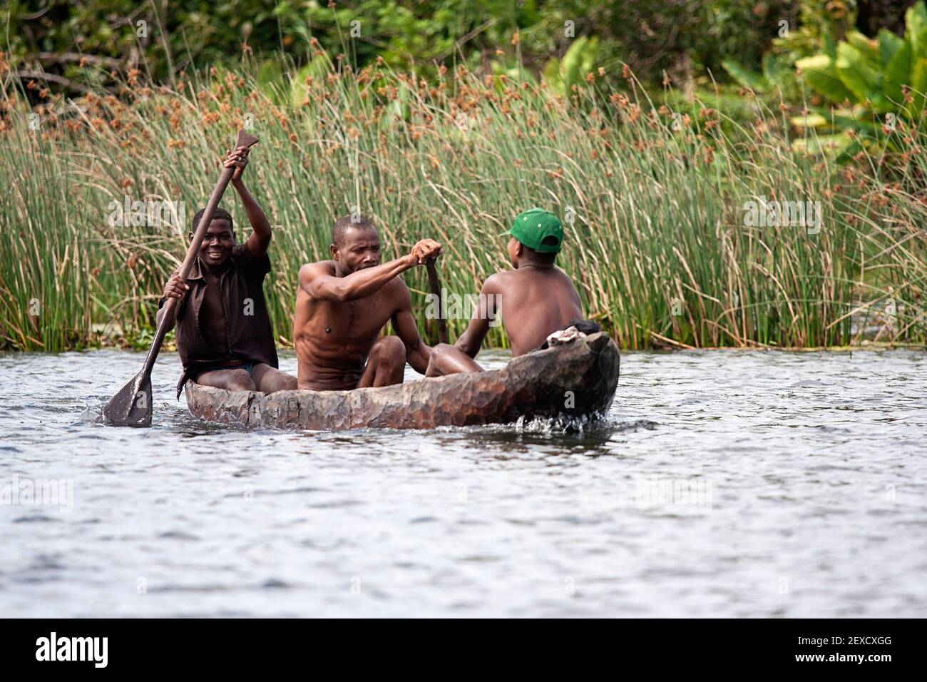 Three men paddling in traditional handmade wooden pirogue canoe ...