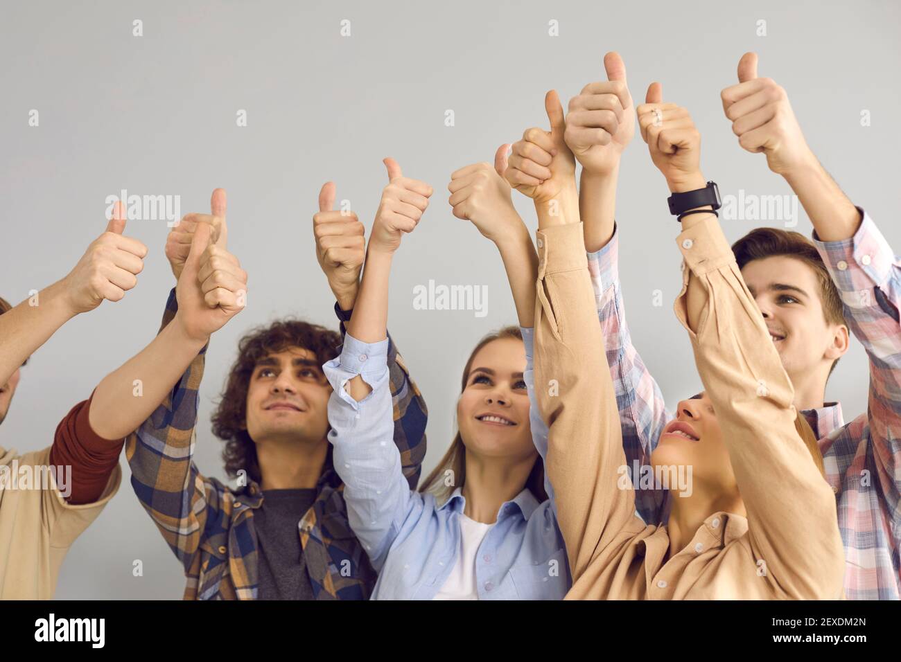 Group of happy young men and women raising hands and giving thumbs-up ...
