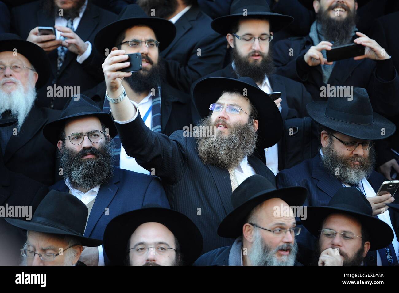 A Rabbi takes a selfie of himself against a see of black hats as ...